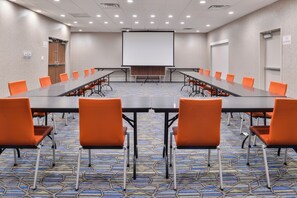 Uma sala de conferências com uma mesa comprida, cadeiras laranja, uma tela de projetor e piso coberto de carpete.