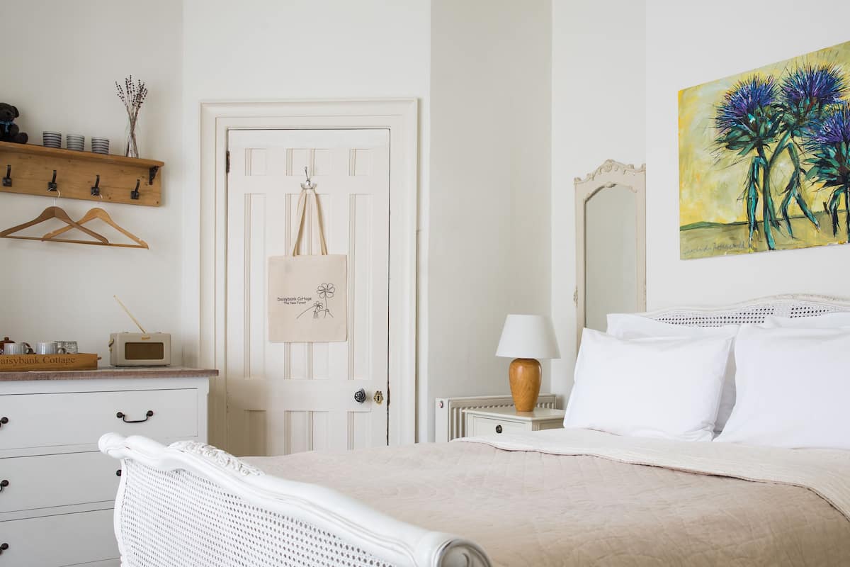 Quarto com cama, mesa de cabeceira, luminária, cômoda e um quadro na parede.