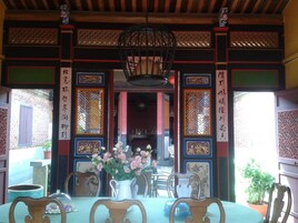 Quarto em estilo tradicional chinês, com mesa posta para refeição, luminária pendente e painéis decorativos com caracteres chineses.