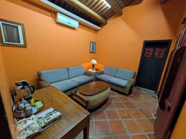 Um quarto aconchegante com um sofá, uma mesa pequena com abajur e piso de azulejos.