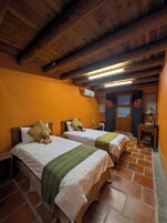 Quarto com duas camas, teto de madeira, paredes laranja e chão ladrilhado.