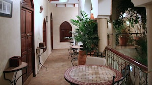 Um corredor com uma mesa redonda e cadeiras, portas de madeira e plantas em vasos.