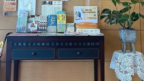 Parede de madeira com caligrafia chinesa e uma mesa com folhetos informativos.