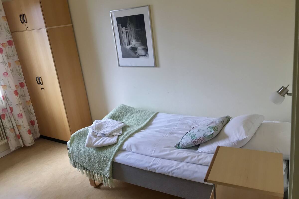 Quarto com cama, guarda-roupa, quadro emoldurado e mesa de cabeceira.
