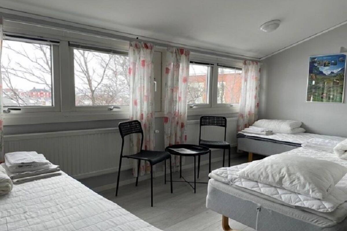 Quarto com duas camas, uma cadeira, uma mesa e um radiador.