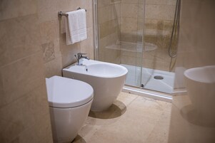 Casa de banho com sanita, bidé e cabine de duche com paredes de vidro.
