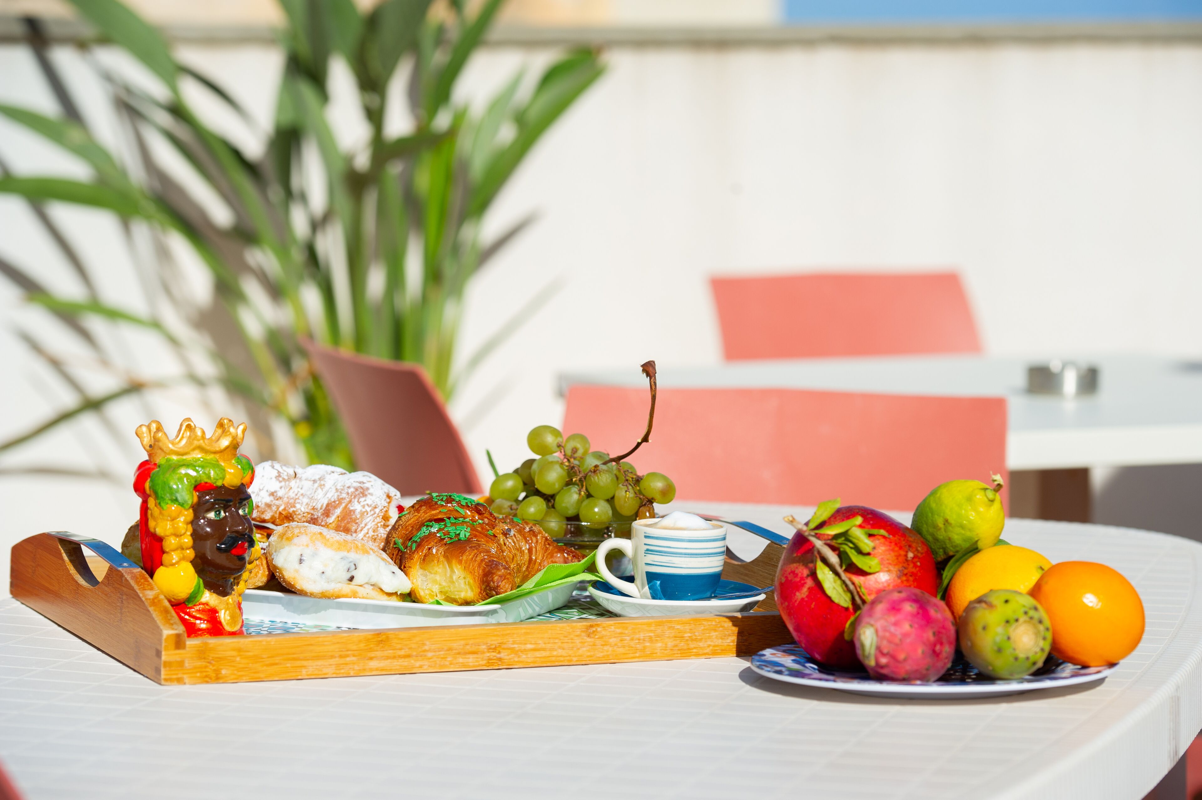 Uma mesa com um croissant, uma xícara de café, uma tábua de frutas e uma peça decorativa.