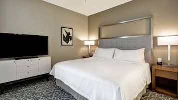 Quarto de hotel com cama, televisão, mesa de cabeceira, abajur e ventoinha de teto.