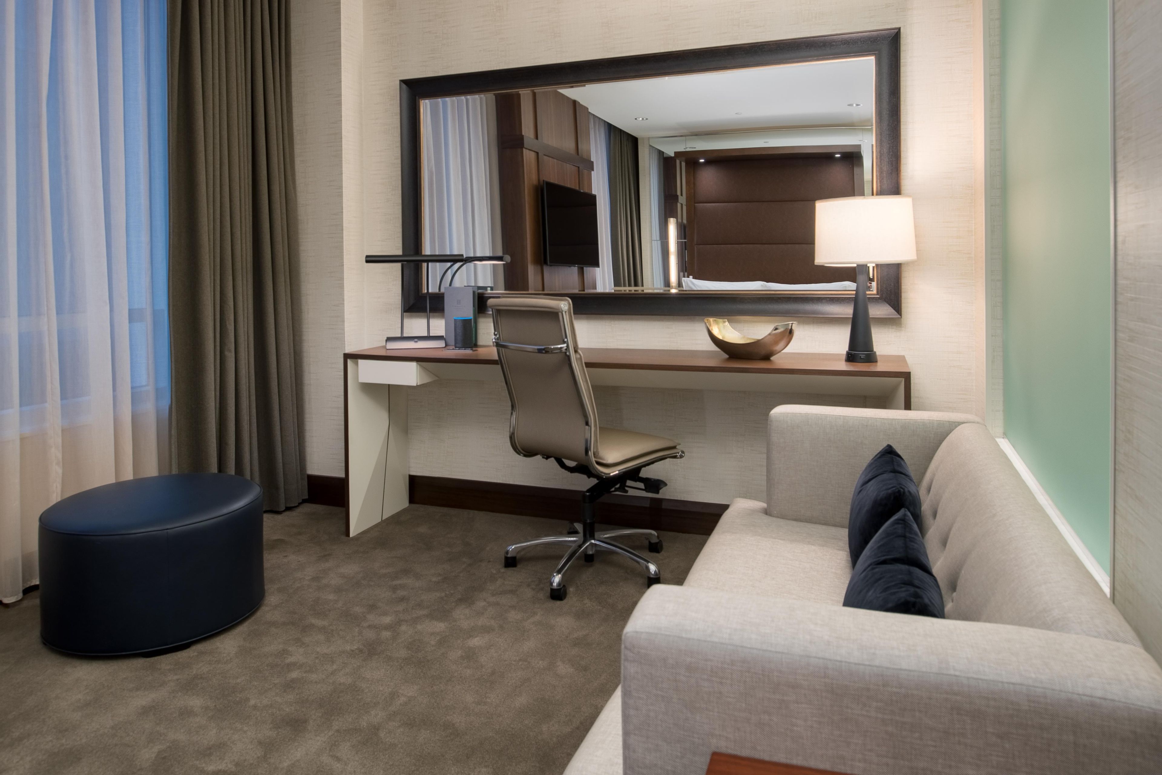 Quarto de hotel com escrivaninha, cadeira, sofá, banquinho e espelho.