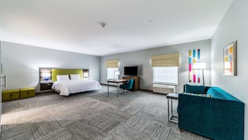Quarto de hotel com cama, escrivaninha, cadeira, televisão e sofá.
