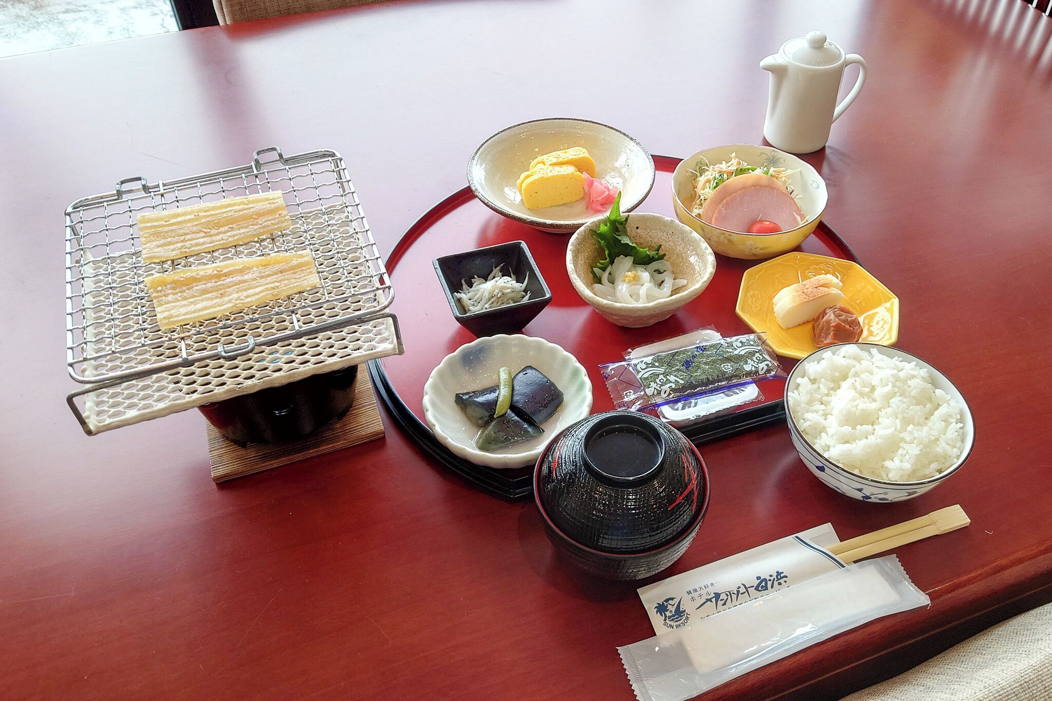 Disposição tradicional de refeição japonesa com diversos pratos e utensílios sobre uma mesa de madeira.