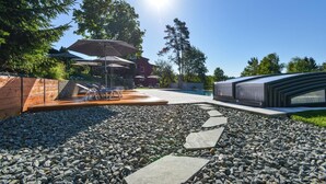 Uma área de piscina com um caminho de pedra, espreguiçadeiras e guarda-sóis.