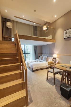 Quarto de hotel com cama beliche, escada de madeira, escrivaninha com cadeira e mesa de cabeceira.