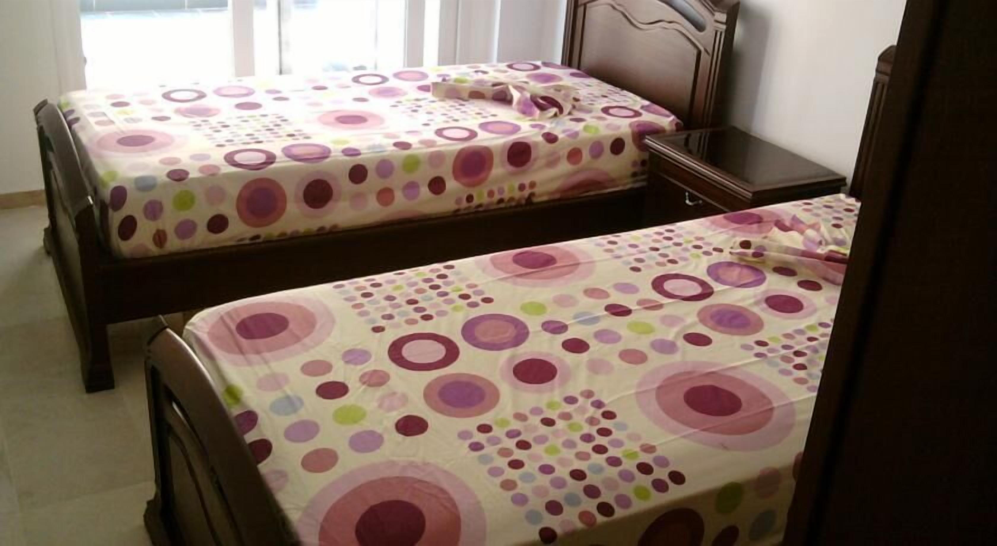 Duas camas de solteiro com cabeceiras e peseiras combinando, cobertas com roupa de cama listrada em bolinhas.