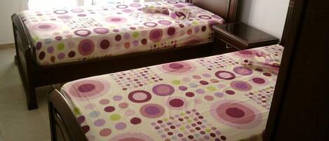 Duas camas de solteiro com cabeceiras e peseiras combinando, cobertas com roupa de cama listrada em bolinhas.