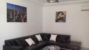 Uma sala de estar moderna com um sofá seccional de couro preto, uma mesa de centro de vidro e duas obras de arte nas paredes.