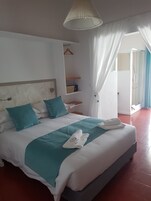Cama bem arrumada com detalhe em verde-água, almofadas brancas e uma toalha branca dobrada sobre a cama.