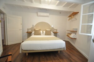 Quarto bem organizado com cama, mesas de cabeceira, luminária pendente e prateleira embutida com toalhas.