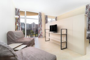 Uma sala de estar moderna com sofá, televisão em móvel e varanda com cortinas.