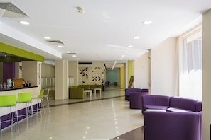 Um saguão moderno com balcão de atendimento, assentos em tons de verde e roxo, e parede estampada.