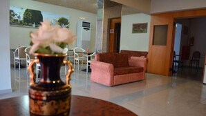 Um saguão de hotel com uma mesa redonda, um vaso com flores, um sofá rosa e uma cadeira branca.