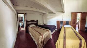 Quarto com duas camas, uma cabeceira de madeira, um guarda-roupa de madeira e uma porta que dá para outro cômodo.