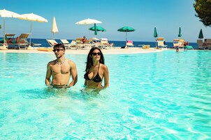 Uma área de piscina com água azul cristalina, espreguiçadeiras e guarda-sóis.