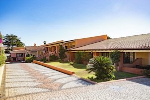 Um pátio com calçada pavimentada, palmeiras e um edifício com telhado em telhas.