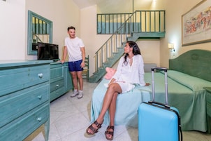 Quarto com uma cama, uma mala, uma televisão e uma escada.