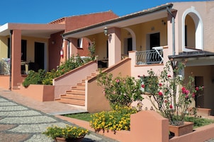 Uma fileira de edifícios em estilo mediterrâneo, com paredes revestidas de estuque, telhados de terracota e um pátio pavimentado.