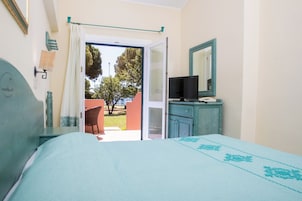 Quarto com cama, televisão sobre uma cômoda e vista para o exterior.