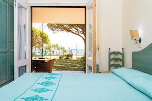 Quarto com cama, vista para uma praia e área de refeições com assentos externos.