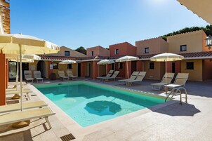 Uma área de piscina com espreguiçadeiras e guarda-sóis, cercada por edifícios com telhados de cerâmica.