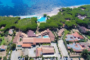 Vista aérea de um resort com piscina cercada por vegetação exuberante, praia e estacionamento.