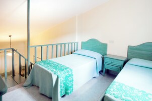 Quarto com duas camas, uma mesinha de cabeceira e escadas.