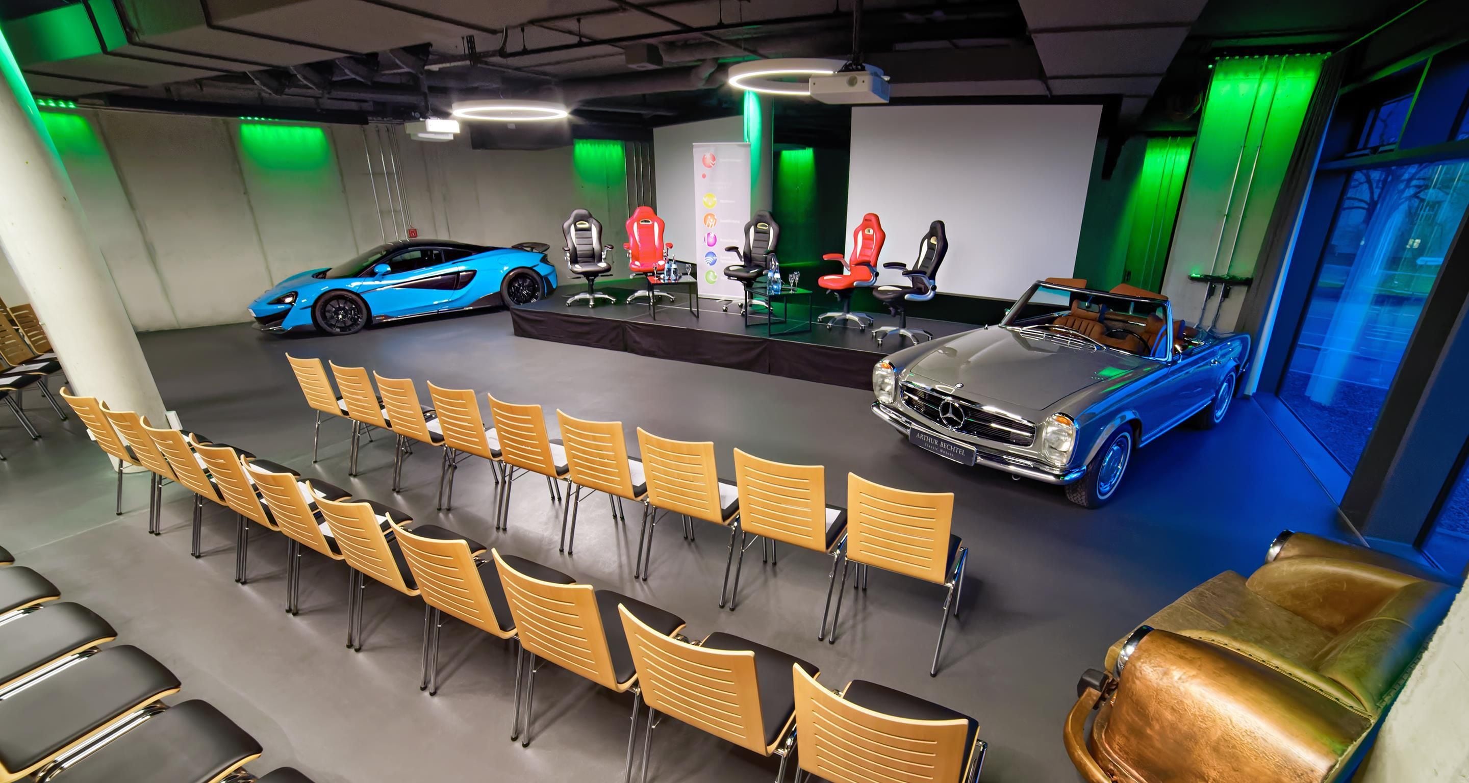 Um showroom com fileiras de cadeiras, um palco com exposição de carros e um carro antigo.