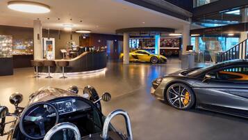 Interior moderno com balcão de recepção, área de estar e exposição de carros de luxo.