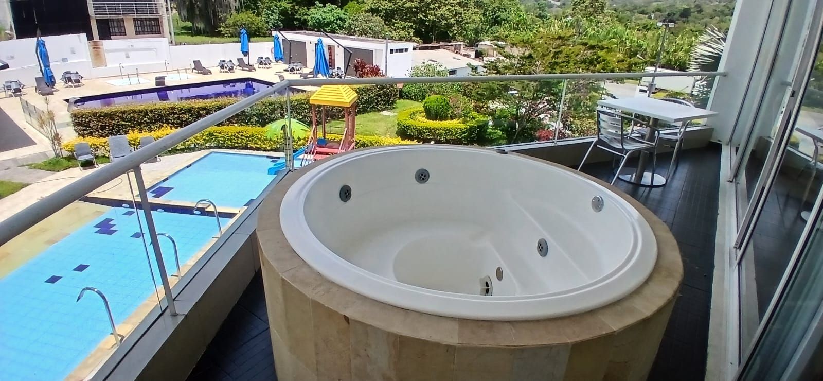 Uma banheira de hidromassagem numa varanda com vista para uma piscina e zona de estar ao ar livre.