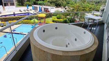 Uma banheira de hidromassagem numa varanda com vista para uma piscina e zona de estar ao ar livre.
