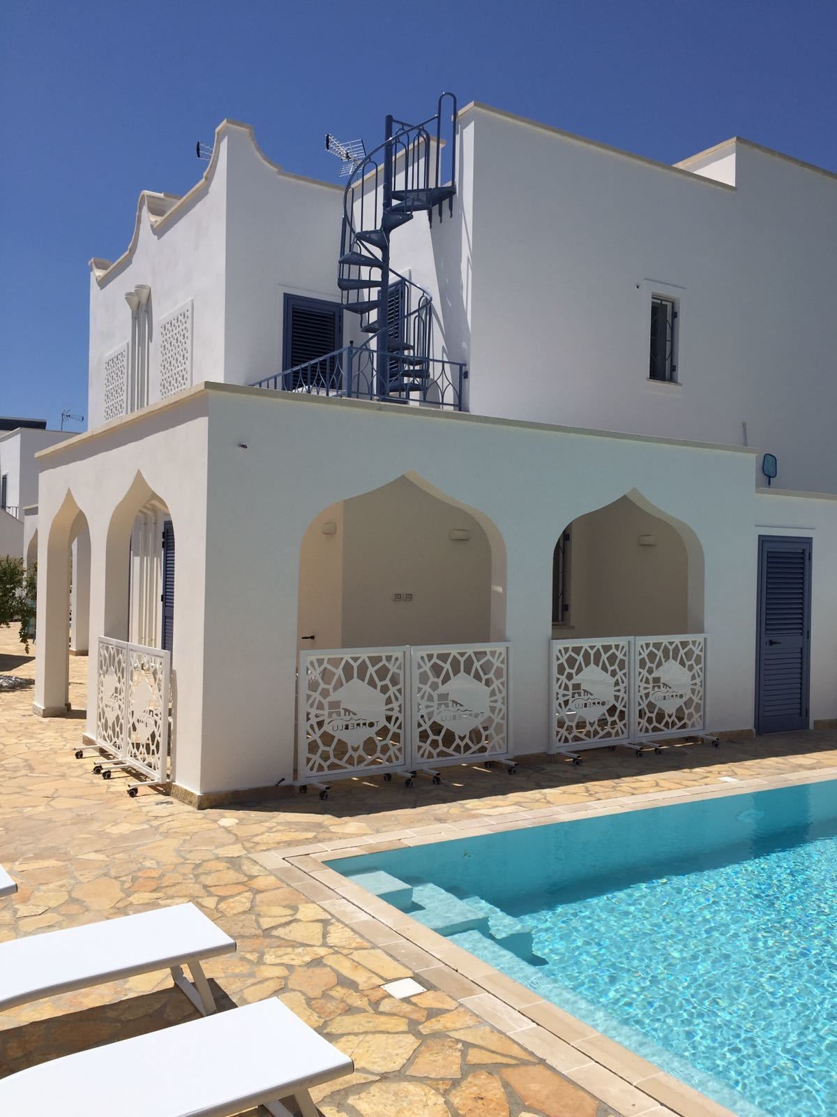 Um edifício branco com piscina, escadaria e área de pátio coberta.
