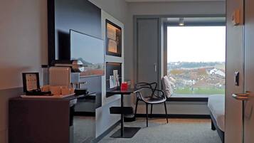 Quarto de hotel com escrivaninha, cadeira, cama e uma grande janela com vista para a cidade.