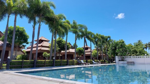 Piscina com espreguiçadeiras, palmeiras e edifícios de estilo tradicional ao fundo.