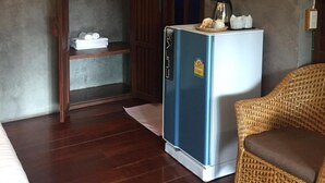 Quarto compacto com geladeira azul, cadeira de vime, televisão fixada na parede e porta de madeira com painel de vidro.