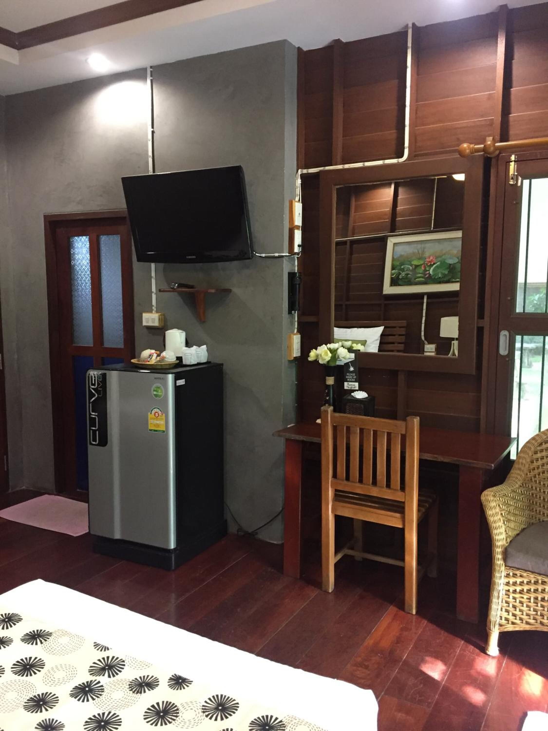 Quarto compacto com geladeira, televisão na parede, uma cadeira de madeira e uma mesa pequena.