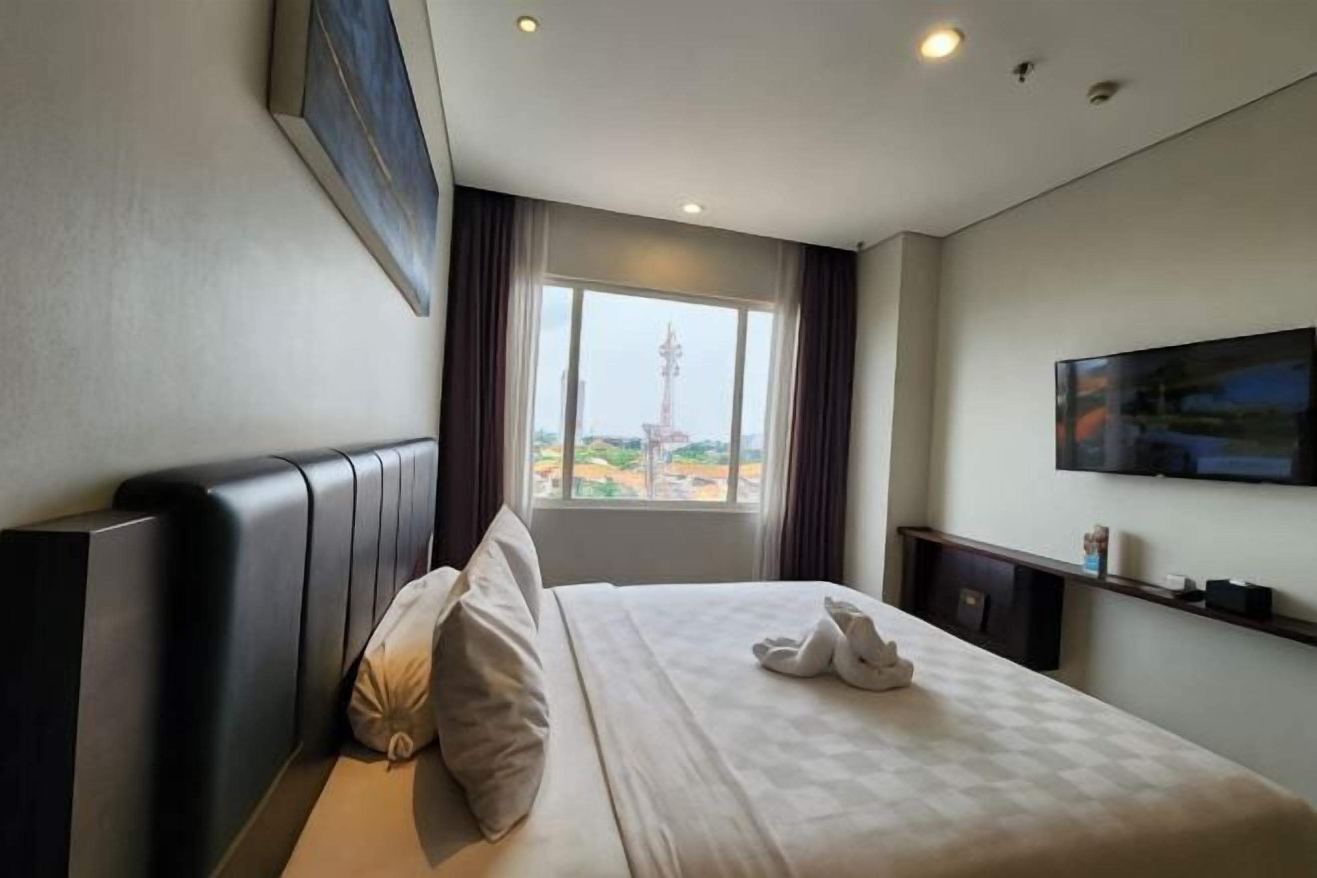 Quarto de hotel com cama, janela com vista, televisão e um quadro na parede.