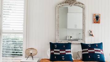 Quarto com cama, mesa de cabeceira, espelho e janela com persianas.
