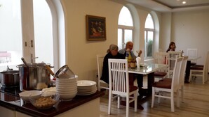 Uma área de refeições com cadeiras brancas, uma mesa e diversos utensílios de cozinha, como panelas e tigelas.