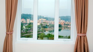 Janela com três painéis, cortinas e vista para uma cidade com edifícios e um rio.