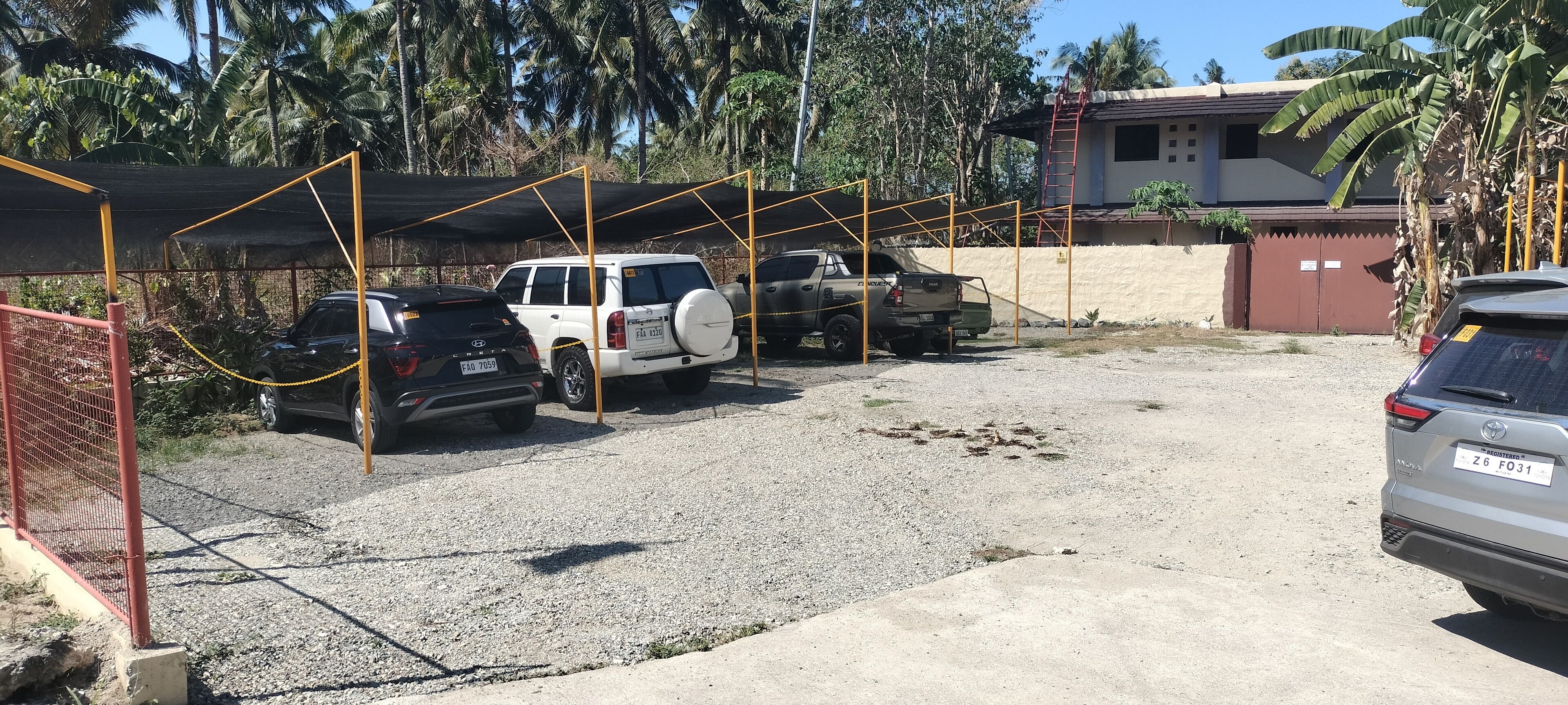 Um estacionamento com vários veículos, incluindo dois SUVs, um branco e outro preto, e um edifício com telhado vermelho ao fundo.