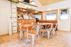 Interior de restaurante com mesas de madeira e cadeiras brancas, um balcão com cardápio e uma placa com a inscrição 'SEABREEZE'.